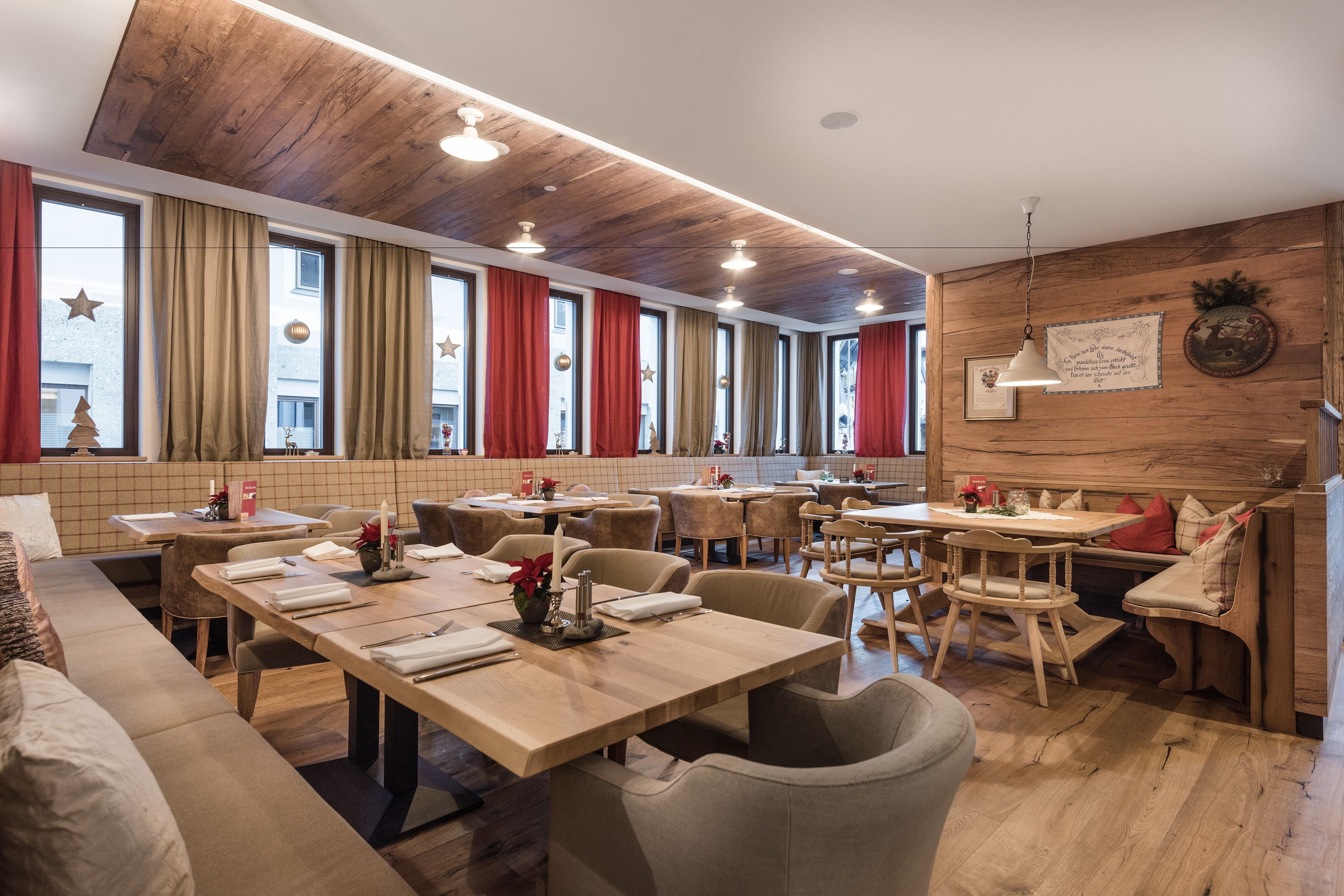Restaurante com teto de madeira, várias mesas e cadeiras, e janelas amplas com cortinas.