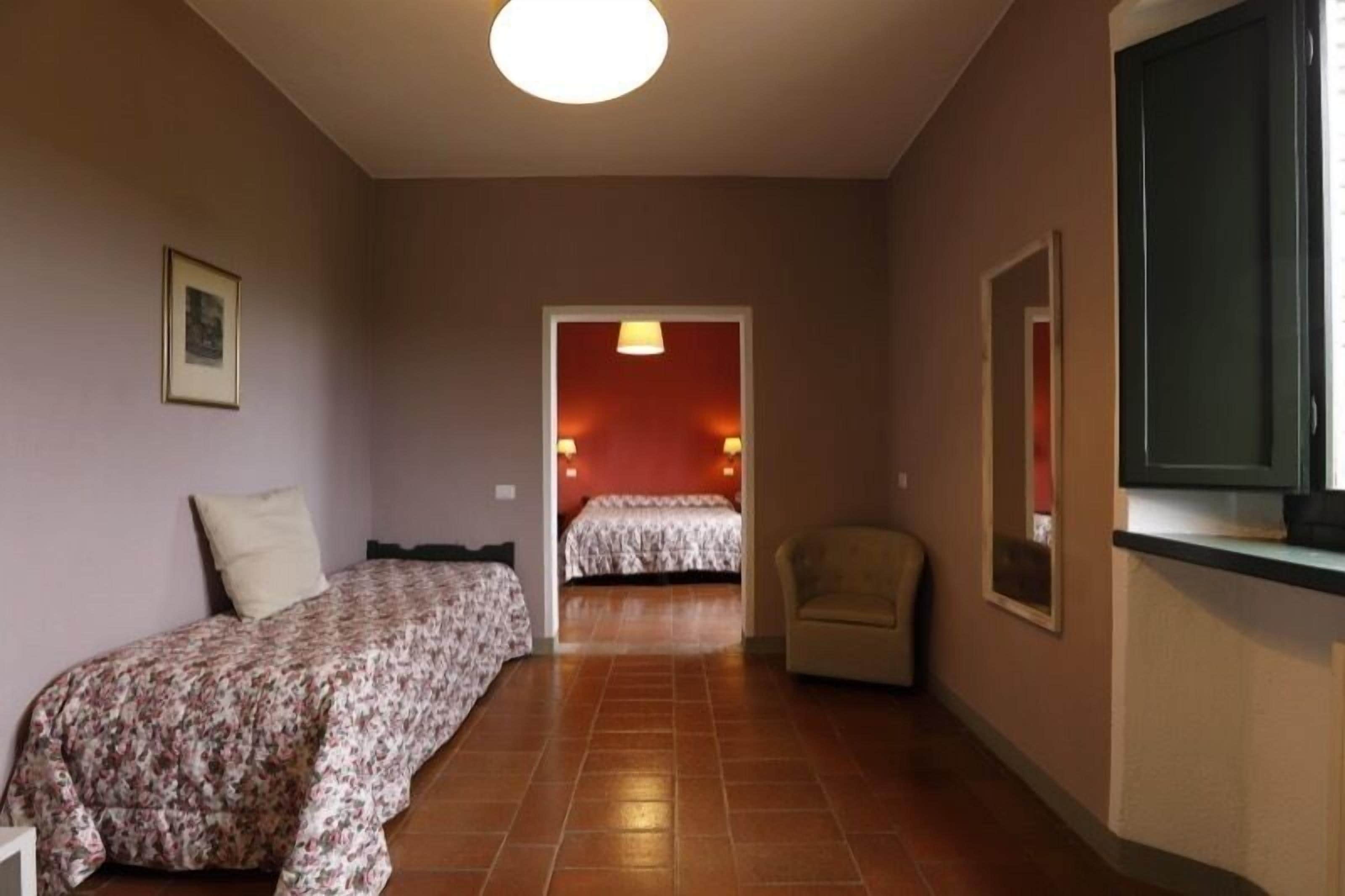Quarto de hotel com cama, uma cadeira, televisão e um quadro na parede.
