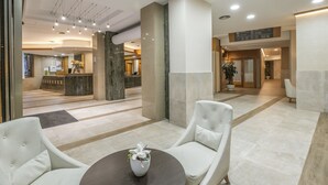 Um saguão de hotel com balcão de recepção, área de estar e sinalização indicando a localização do restaurante e da piscina.