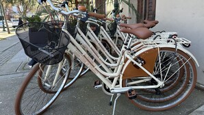 Uma bicicleta com cesto e selim marrom estacionada na calçada.
