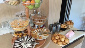 Buffet com diversas opções de comida, incluindo frutas, cereais, pães e um bolo.