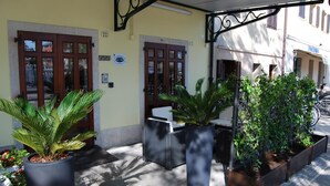Entrada de um edifício com duas portas, plantas em vasos e mesas ao ar livre.