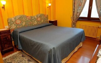 Quarto com cama, mesas de cabeceira de madeira, tapete estampado e janela com cortinas.