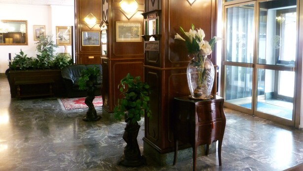 Um hall com piso de mármore, mobiliário de madeira e um vaso com flores.