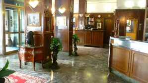 Um hall de entrada com balcão de recepção, painéis de madeira, piso de mármore e tapete vermelho.