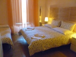 Quarto de hotel com cama, uma cadeira, abajur e janela com cortinas.