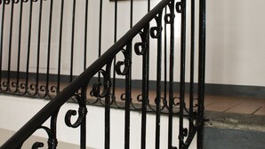 Uma escadaria com grades de ferro preto ricamente decoradas e uma parede adornada com diversos espelhos e arandelas.