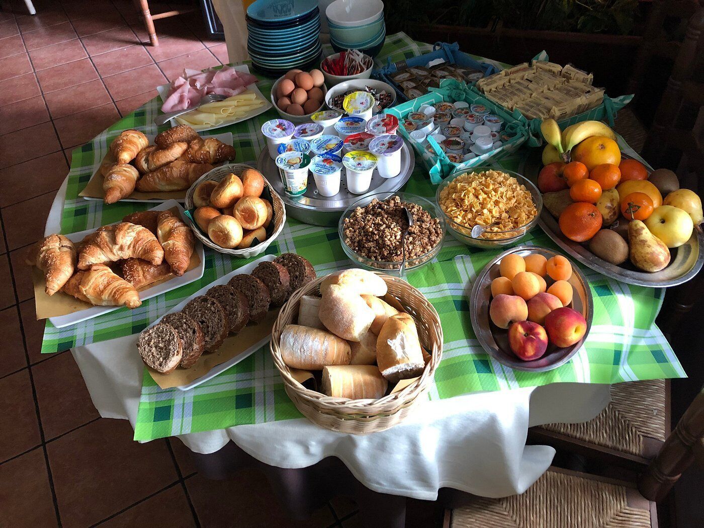 Um buffet de café da manhã com diversos pães, doces, frutas e produtos lácteos.