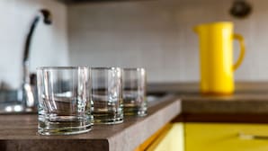 Três copos de vidro transparentes sobre uma bancada de cozinha, com um jarro amarelo ao fundo.
