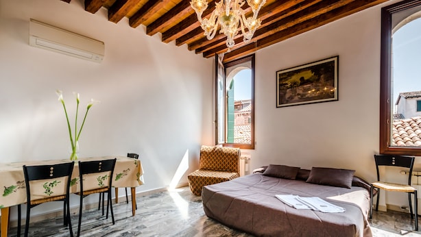 Quarto com cama, mesa de jantar com cadeiras, um candelabro e janela com vista.