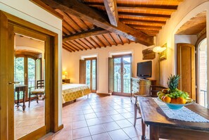 Quarto com cama, mesa de jantar com fruteira, televisão e varanda com vista para o exterior.