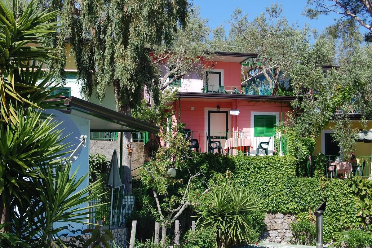 Um edifício de dois andares com varanda, cercado por vegetação exuberante.