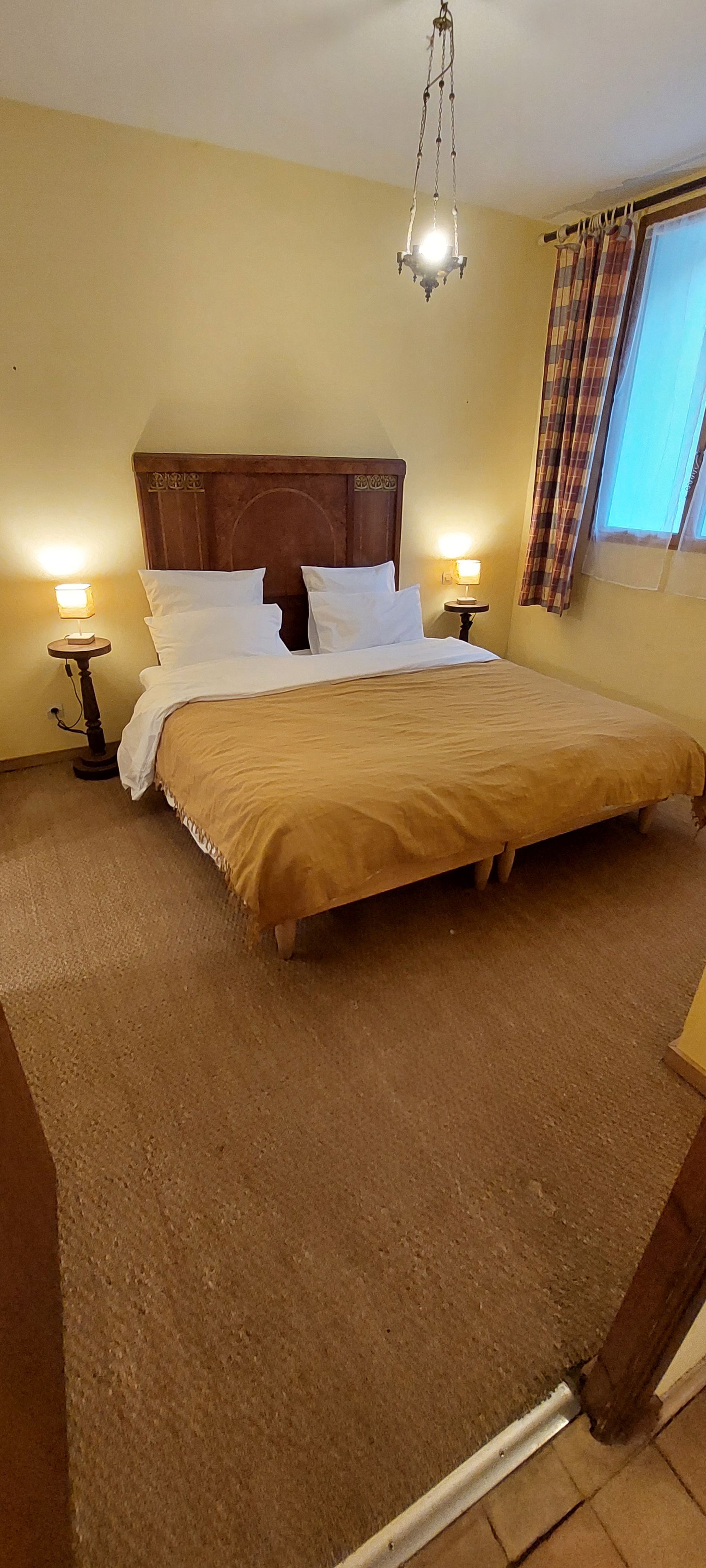 Uma cama com cabeceira de madeira, duas luminárias de apoio e um lustre.