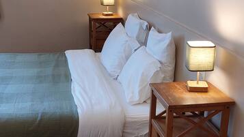 Uma cama de solteiro com estrutura de madeira, duas mesas de cabeceira com abajures e piso de madeira.