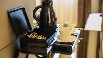 Uma estação de café com uma cafeteira preta, duas chávenas brancas e um suporte com uma caixa preta de cápsulas de café.