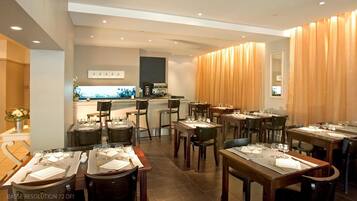 Restaurante com várias mesas preparadas para o serviço, área de bar e vista para a paisagem urbana.