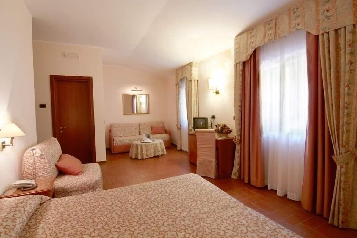 Quarto de hotel com cama, dois sofás, uma mesinha, televisão e cortinas.