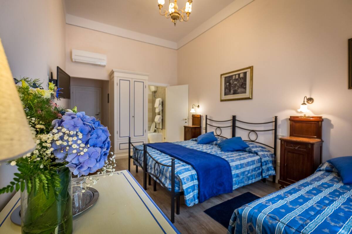 Quarto com duas camas, mesa de cabeceira, abajur e um vaso com flores.