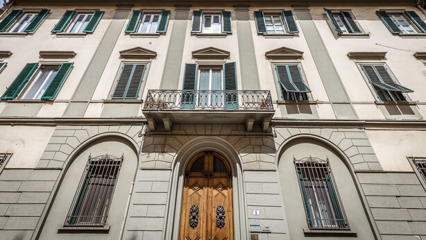 Fachada de edifício com várias janelas, porta de madeira central e varanda com grades de metal.