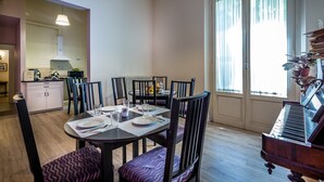 Uma sala de jantar com um piano, cadeiras e uma mesa posta para quatro pessoas.