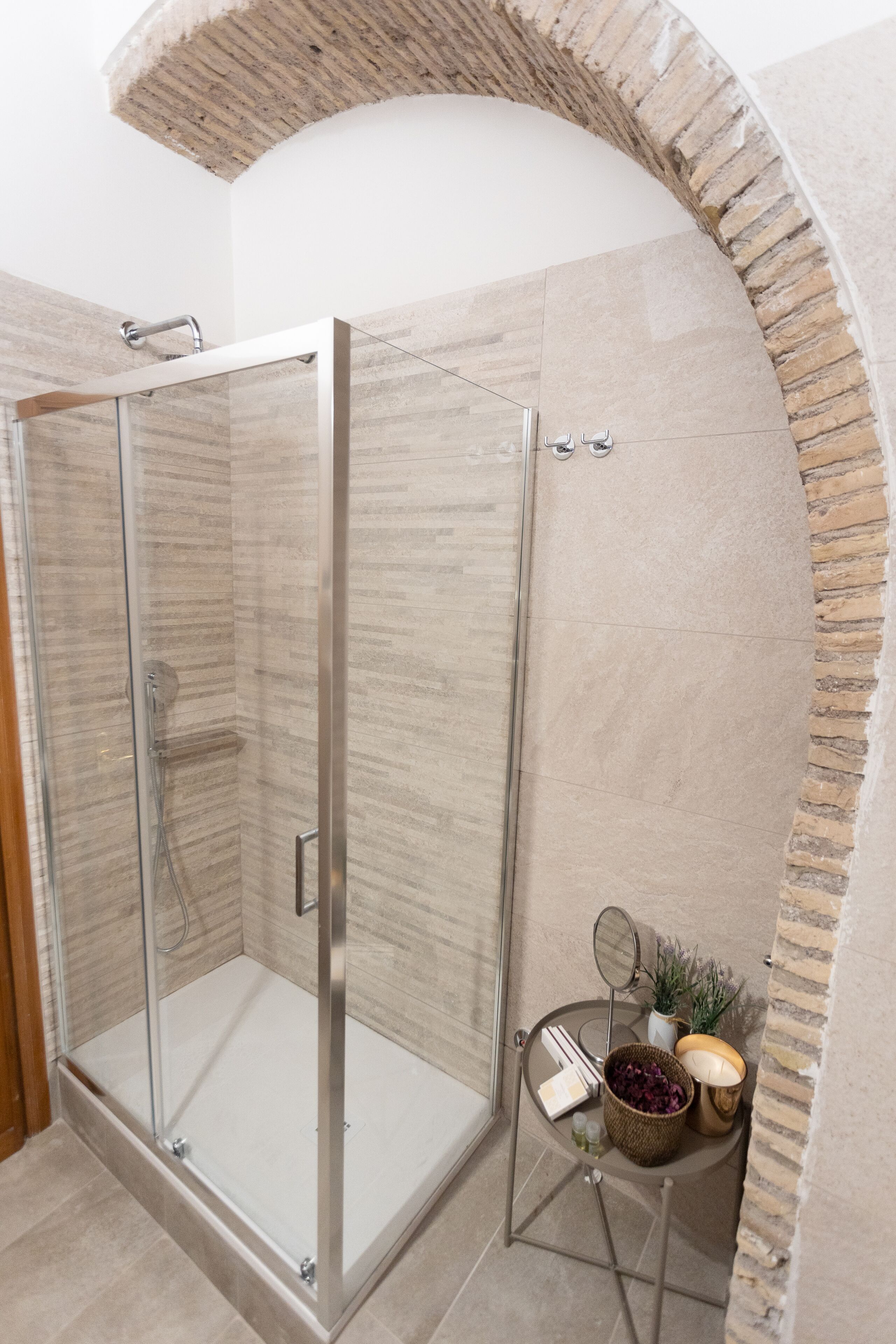 Um chuveiro envidraçado com design moderno, uma pequena mesa com artigos de higiene pessoal e um arco de tijolos.