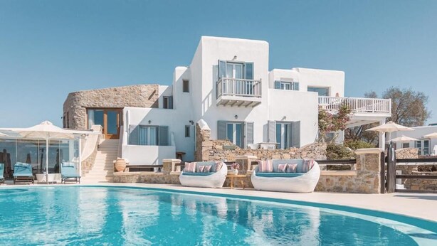 Um edifício moderno e branco, com piscina, paredes de pedra e área externa para sentar.