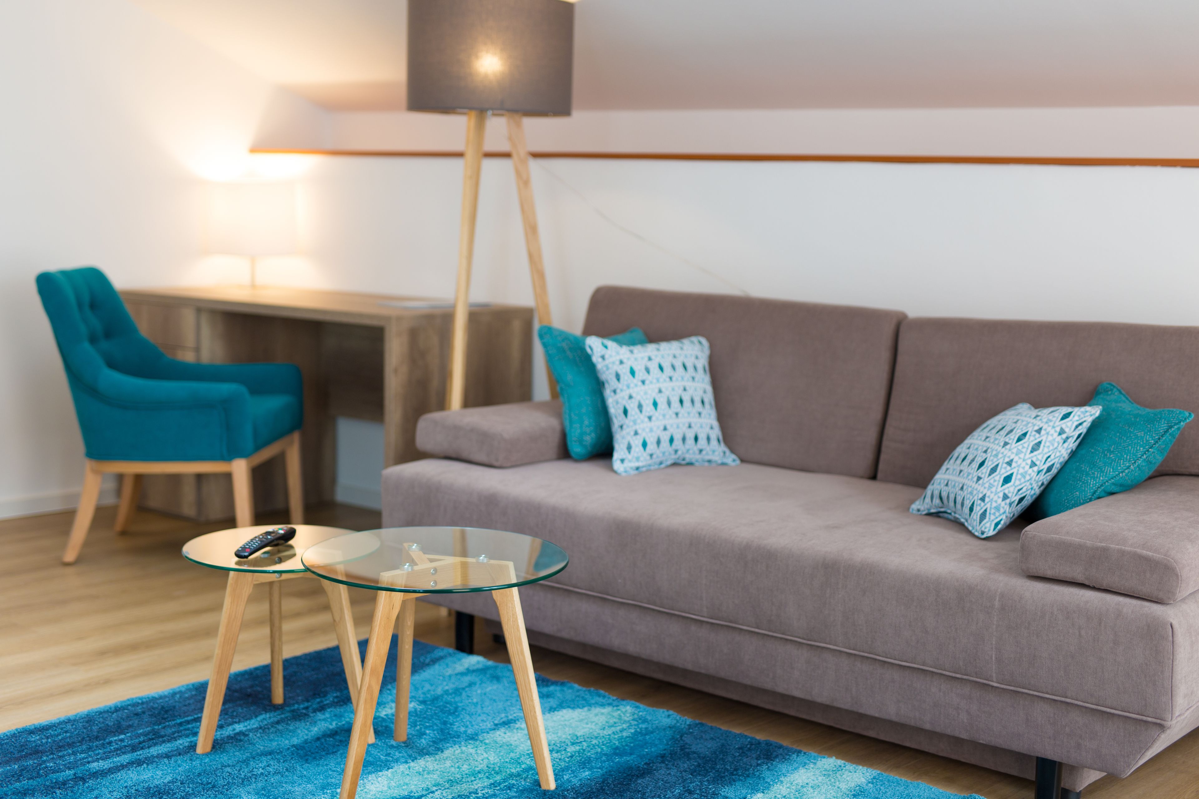 Uma sala de estar moderna com um sofá, uma mesa de centro de vidro, uma poltrona azul-turquesa e um abajur.