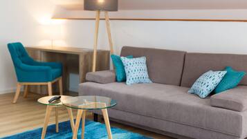 Uma sala de estar moderna com um sofá, uma mesa de centro de vidro, uma poltrona azul-turquesa e um abajur.