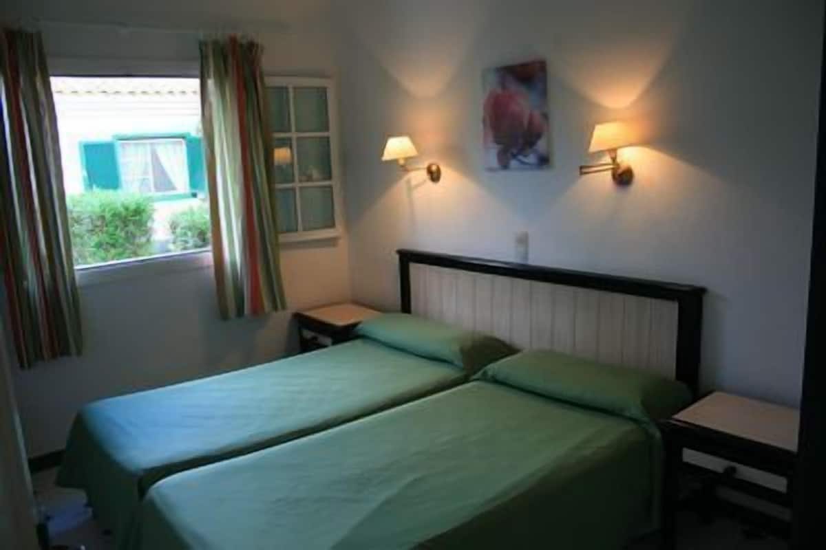 Quarto com duas camas, janela com cortinas, um quadro na parede e duas luminárias de cabeceira.