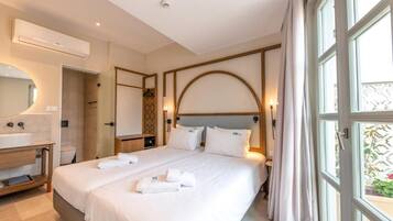 Quarto de hotel com uma cama grande, mesa de cabeceira, espelho, janela com cortinas e ar condicionado.