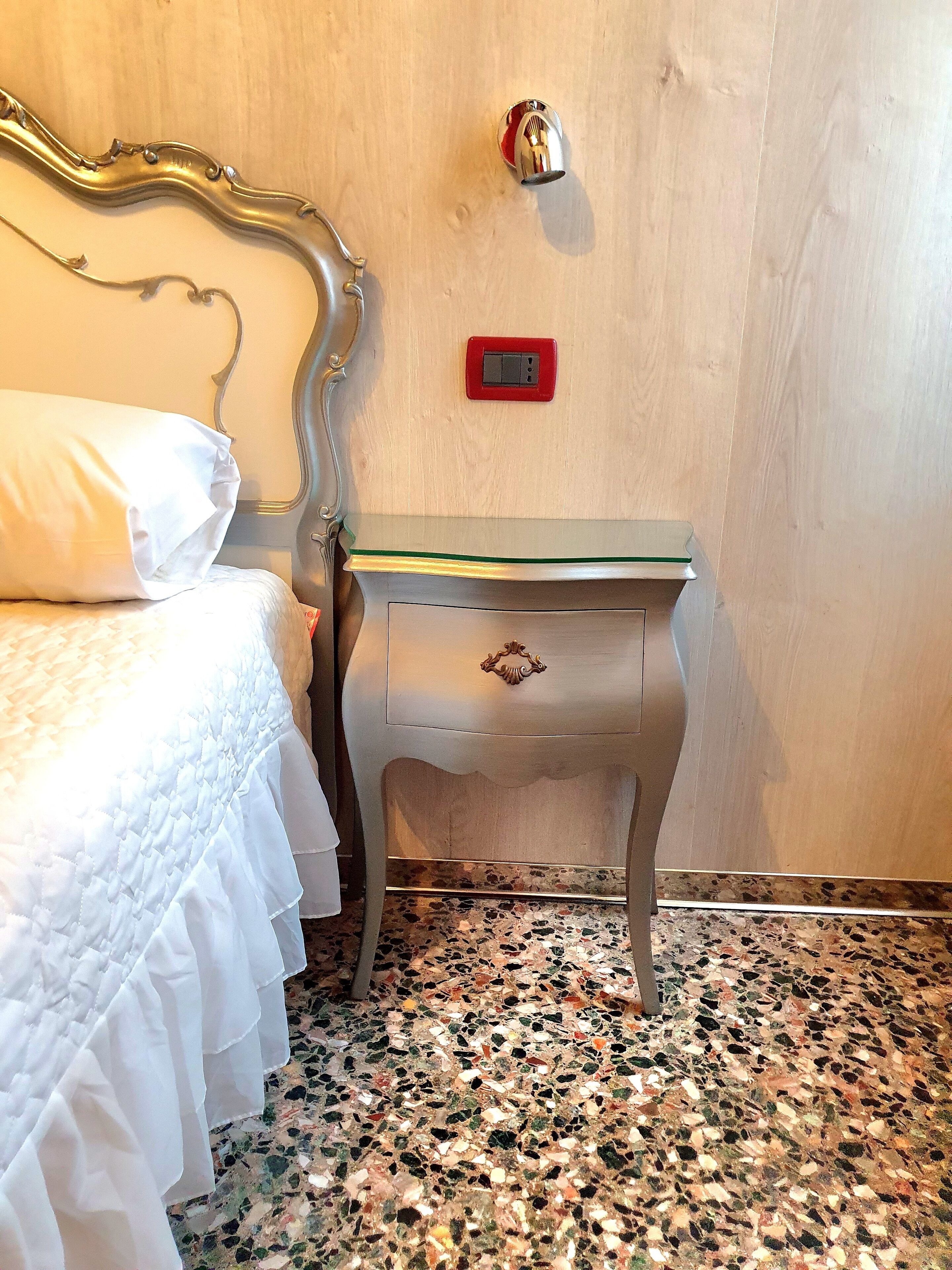 Quarto com cama, mesa de cabeceira, termostato e piso de mármore.