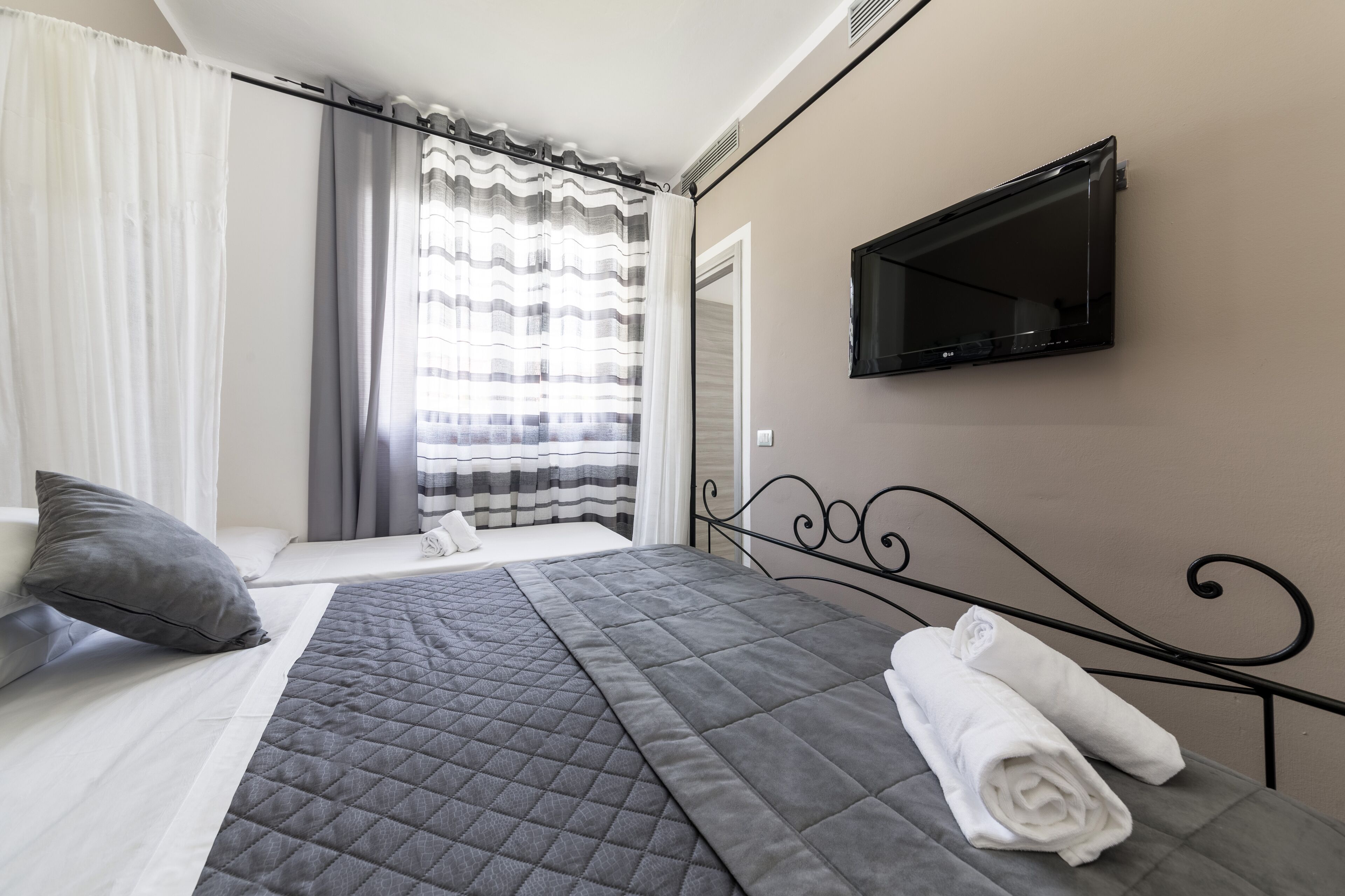 Cama bem arrumada com um cobertor cinza acolchoado, uma toalha branca enrolada e um travesseiro cinza.