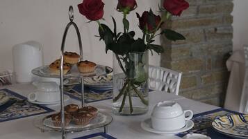 Uma mesa posta com um suporte escalonado para muffins, um bule e um vaso com rosas.