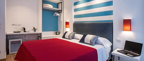 Quarto de hotel moderno com uma cama, uma escrivaninha, um laptop e um tapete vermelho.