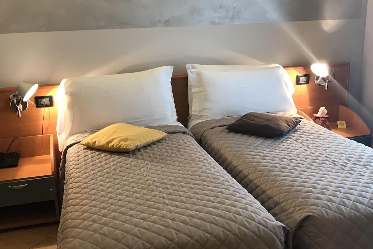 Cama de casal com colcha acolchoada, duas almofadas, abajur e mesa de cabeceira com telefone e caixa de lenços.