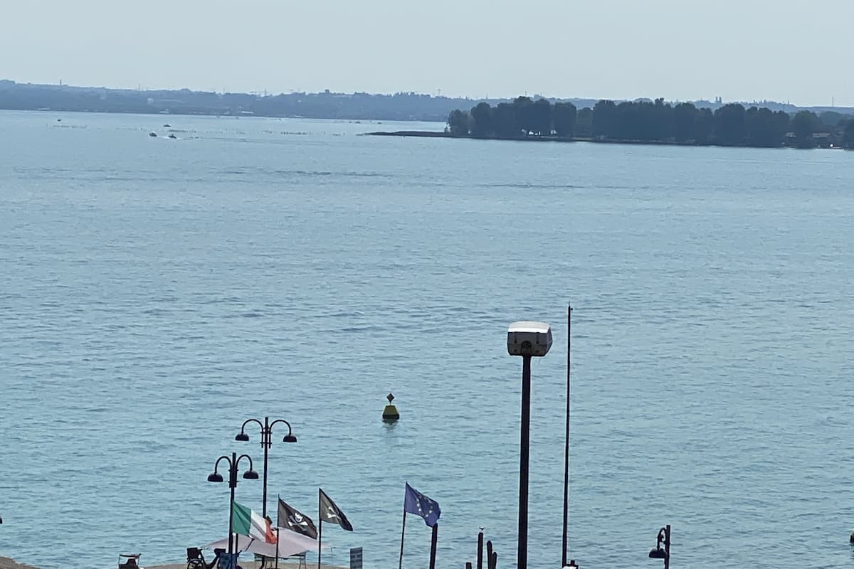 Vista para a orla marítima, com céu claro, águas calmas e horizonte urbano ao longe.