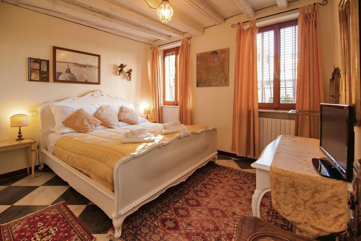 Quarto com cama, mesa de cabeceira, abajur, televisão e tapete estampado.