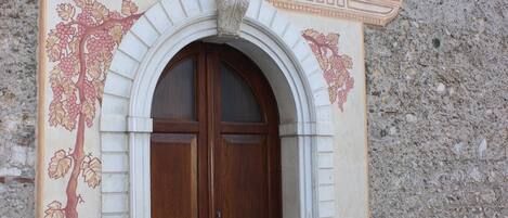 Fachada de edifício com uma grande porta de madeira arqueada, uma janela acima e decoração na parede incluindo uma trepadeira e um leão.