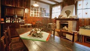 Interior rústico de madeira, com mesa de jantar, cadeiras, lareira e parede decorada com pratos e quadros.