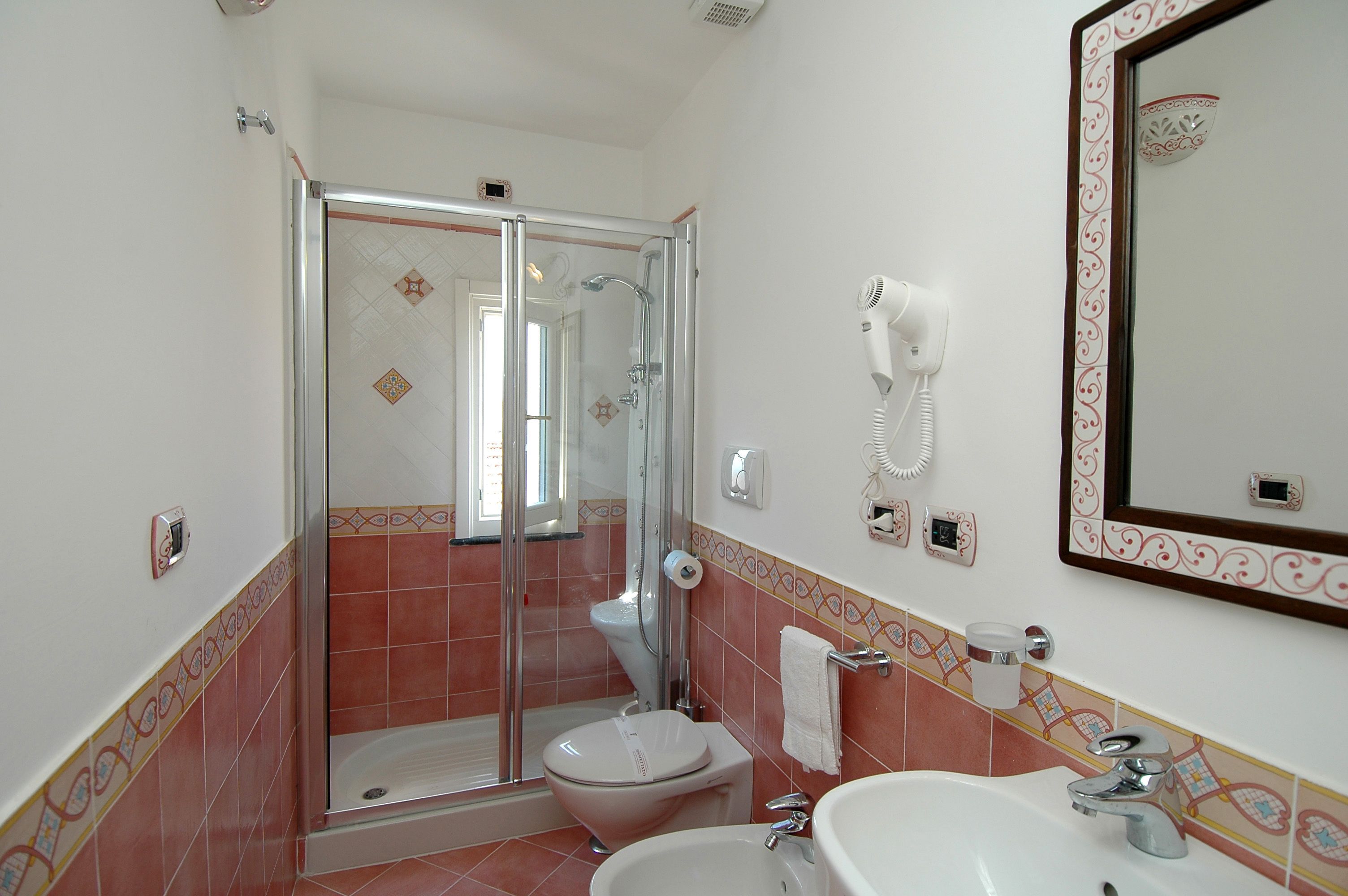 Casa de banho com cabine de duche em vidro, sanita, lavatório e secador de cabelo.