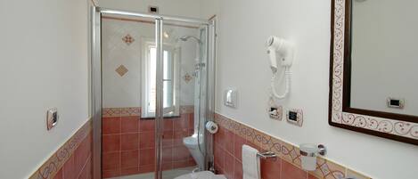 Casa de banho com cabine de duche em vidro, sanita, lavatório e secador de cabelo.