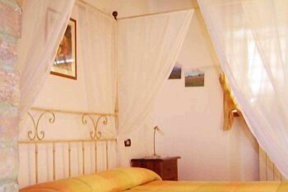 Uma cama com um cobertor amarelo e laranja, uma mesa de cabeceira e um quadro na parede.