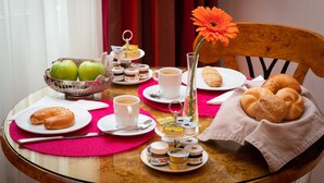 Mesa de café da manhã com pães, uma xícara de café, um vaso com flor e uma tigela de frutas.