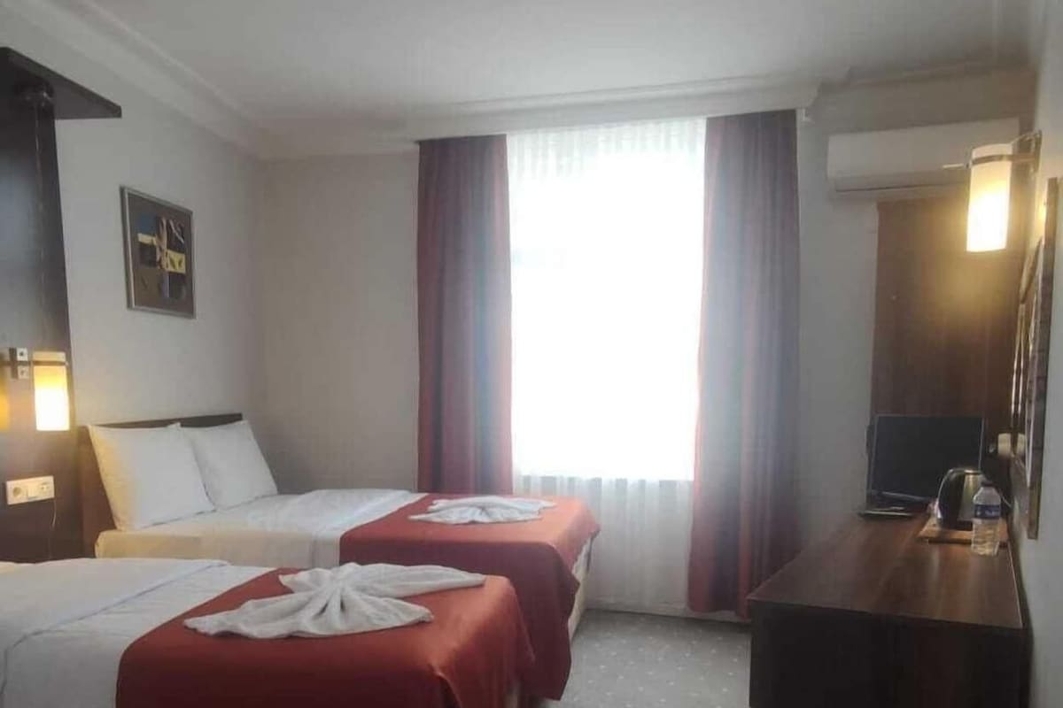 Quarto de hotel com duas camas, uma escrivaninha, uma cadeira, uma televisão e uma janela com cortinas.
