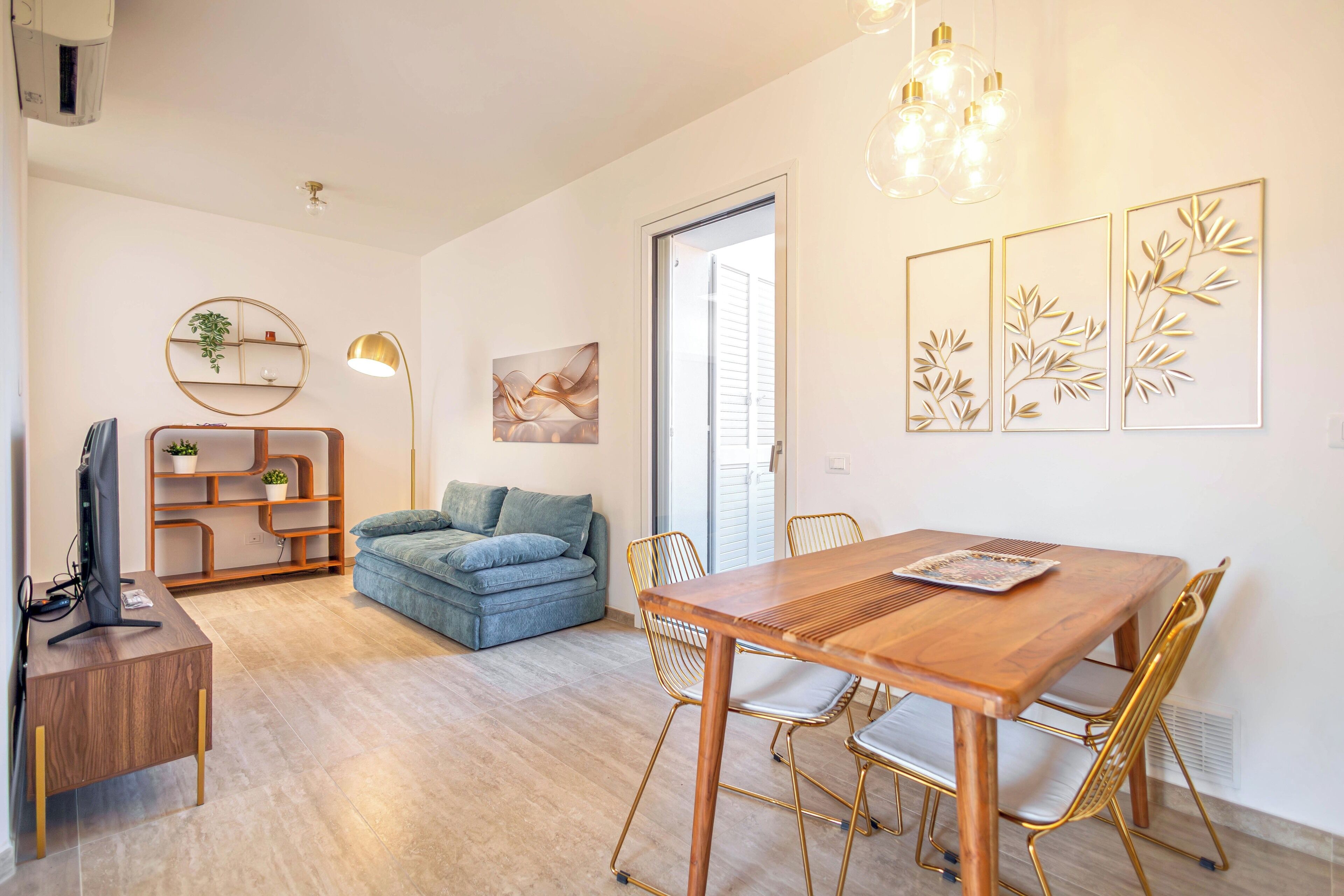 Uma sala de estar moderna com uma mesa de jantar de madeira, um sofá azul, uma TV sobre um móvel de madeira e uma estante com plantas.