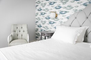 Quarto com cama, poltrona estofada, mesinha redonda e parede com padrão de peixes.