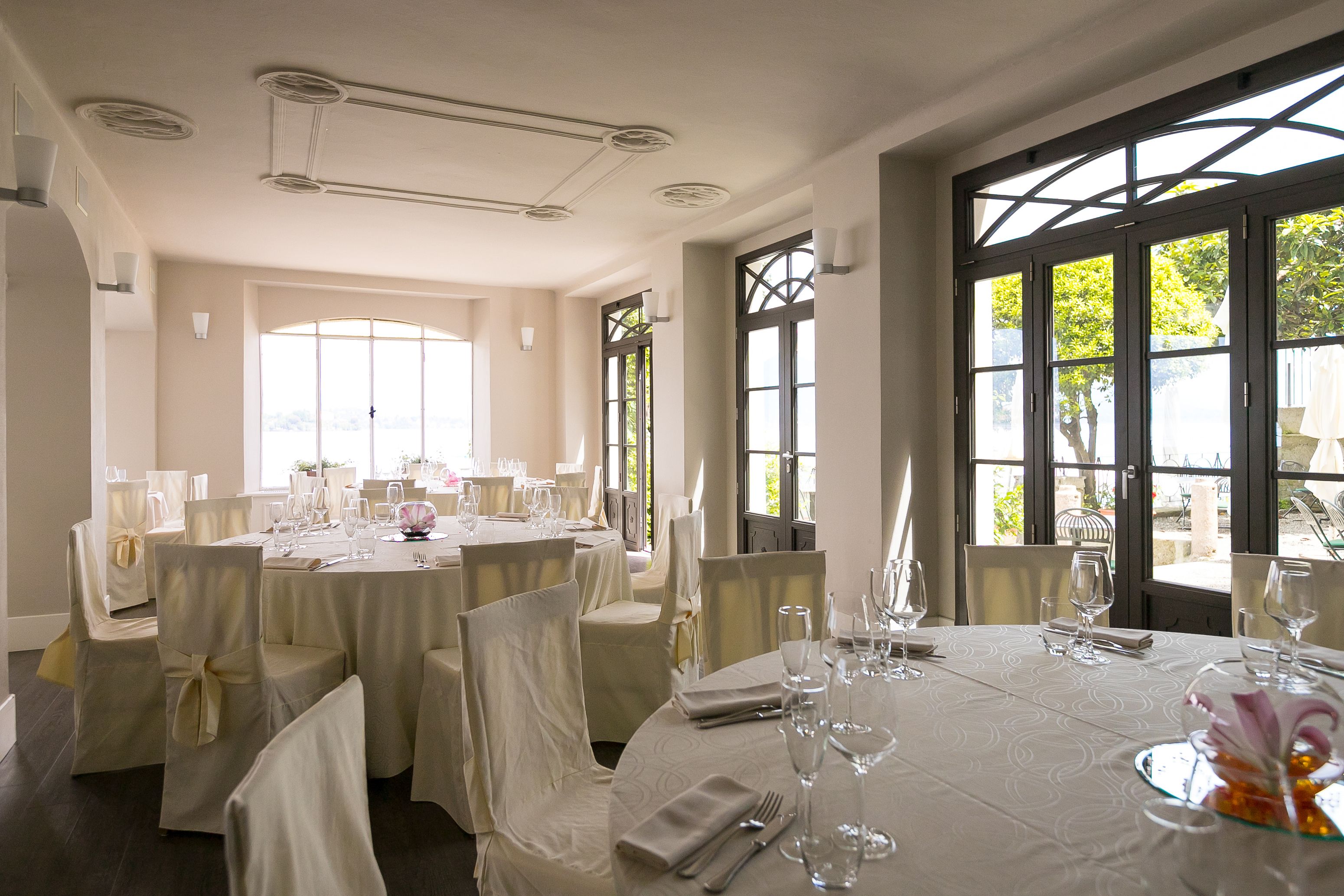 Uma área de refeições com mesas redondas preparadas para um evento formal, com toalhas brancas e cadeiras decoradas com laços.