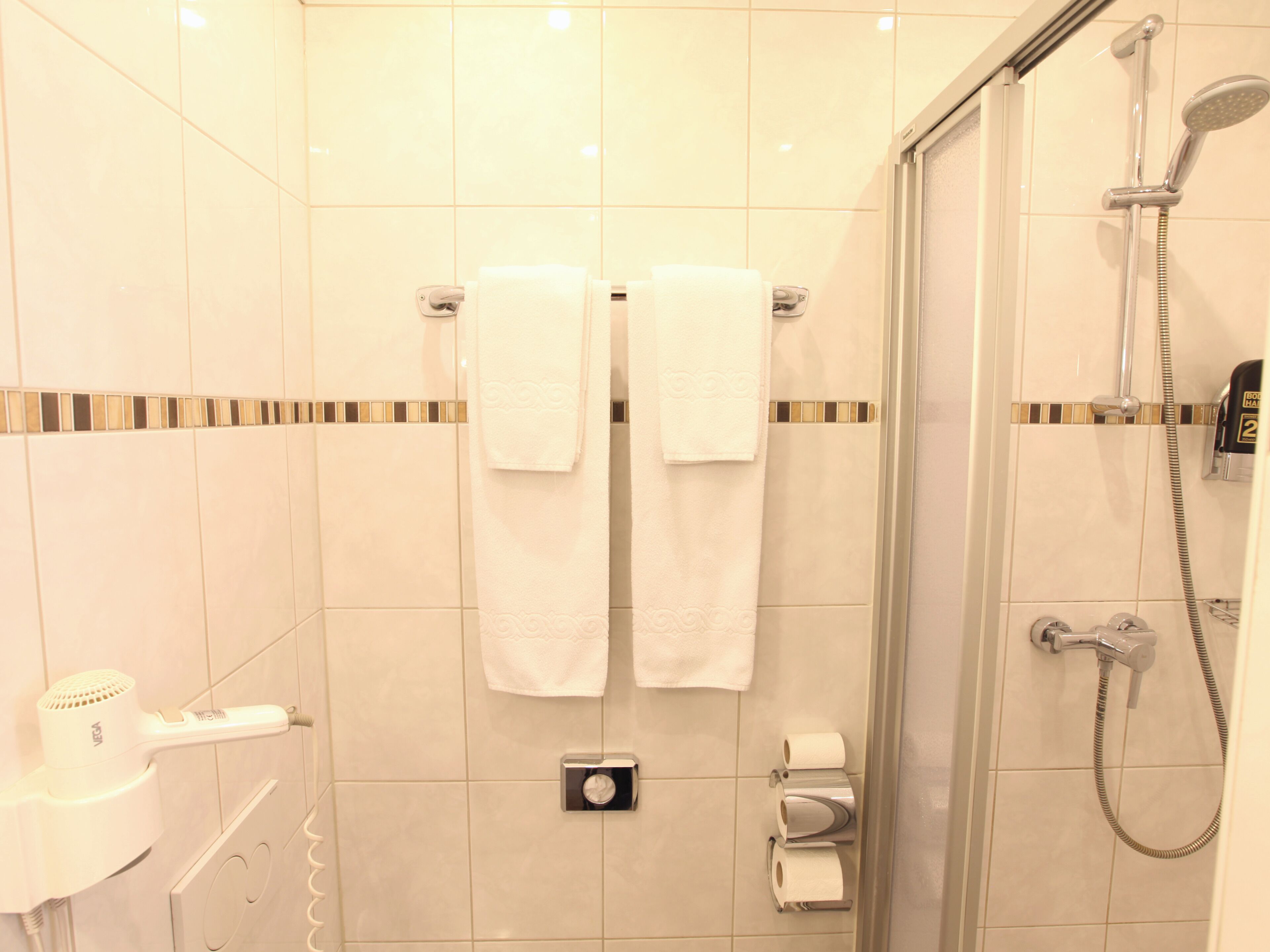 Casa de banho com chuveiro, secador de cabelo e suporte para rolo de papel higiénico.