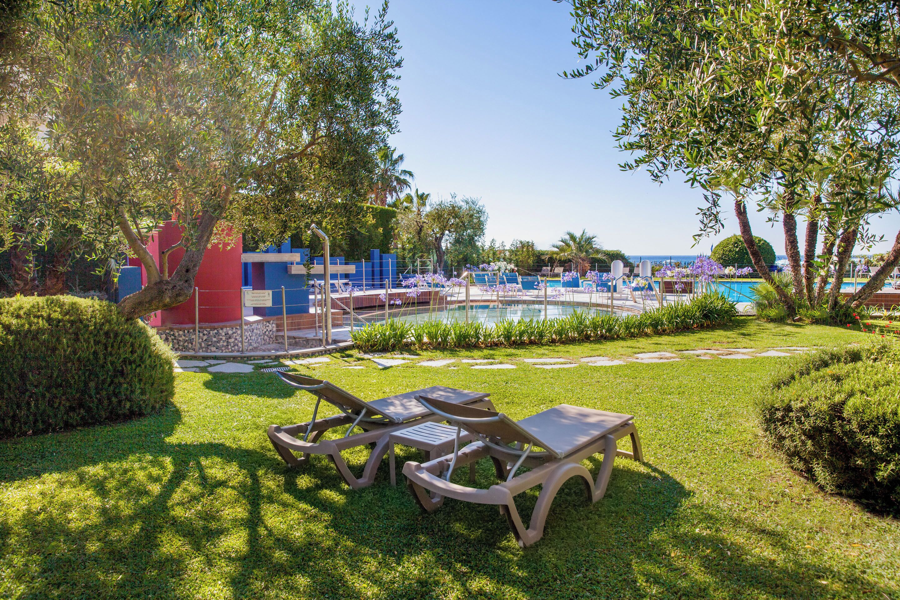 Uma área à beira da piscina com espreguiçadeiras, piscina e vista para o mar.