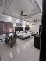 Quarto de hotel com duas camas, uma mesa de jantar e cadeiras, um ventilador de teto e painéis decorativos na parede.